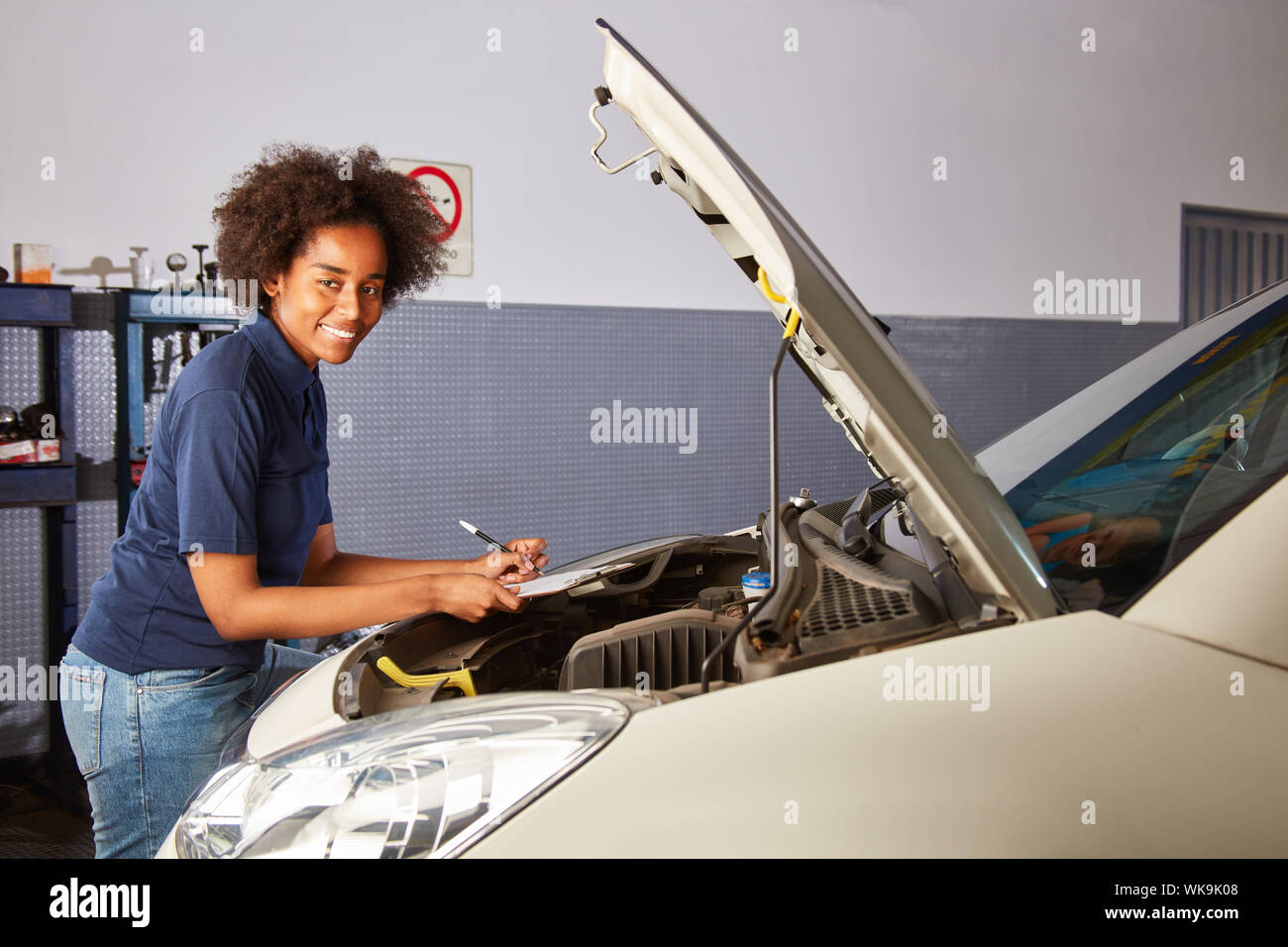 Smiling African woman as a mechatronics apprentice with checklist for ...