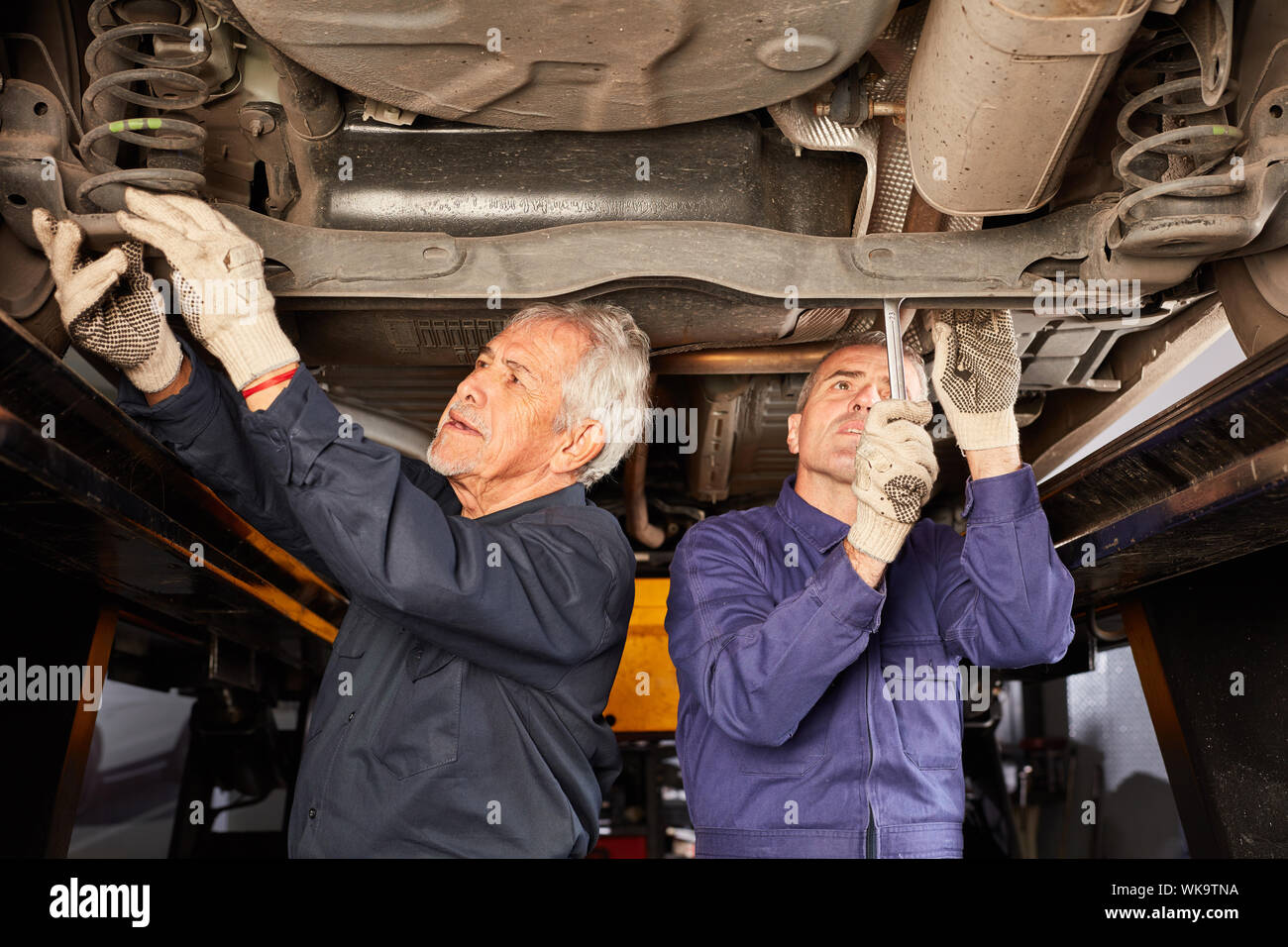 Two mechanics repairing or inspecting a car on the lift Stock Photo - Alamy
