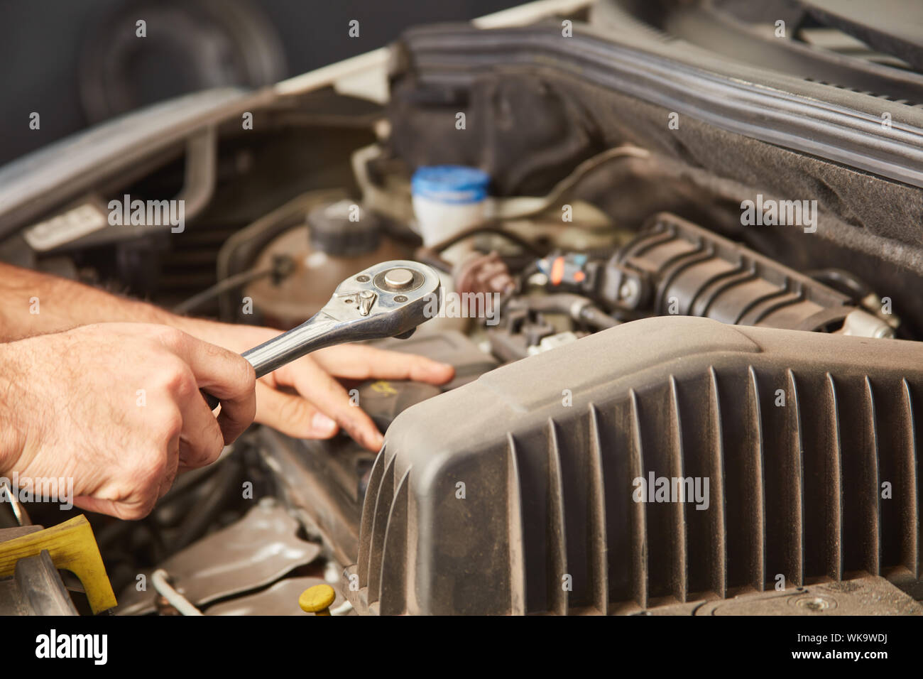 Hand with tool examines engine of car in a workshop during the ...
