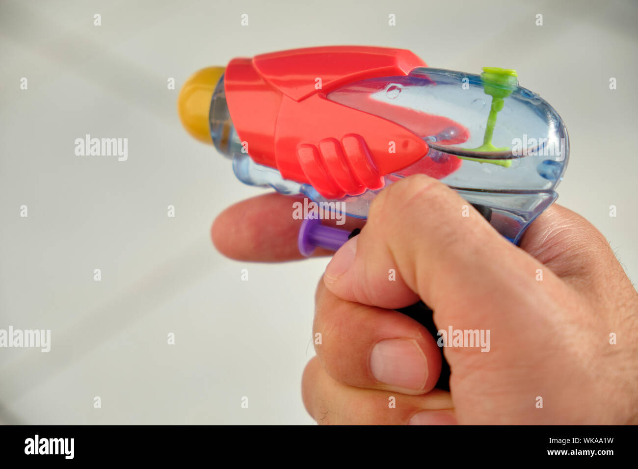A colorful water pistol in a caucasian male hand in front of a white ...