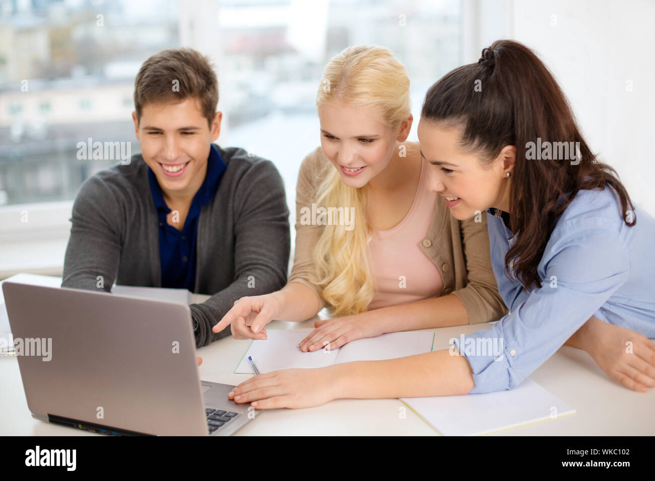 three smiling students with laptop and notebooks Stock Photo - Alamy