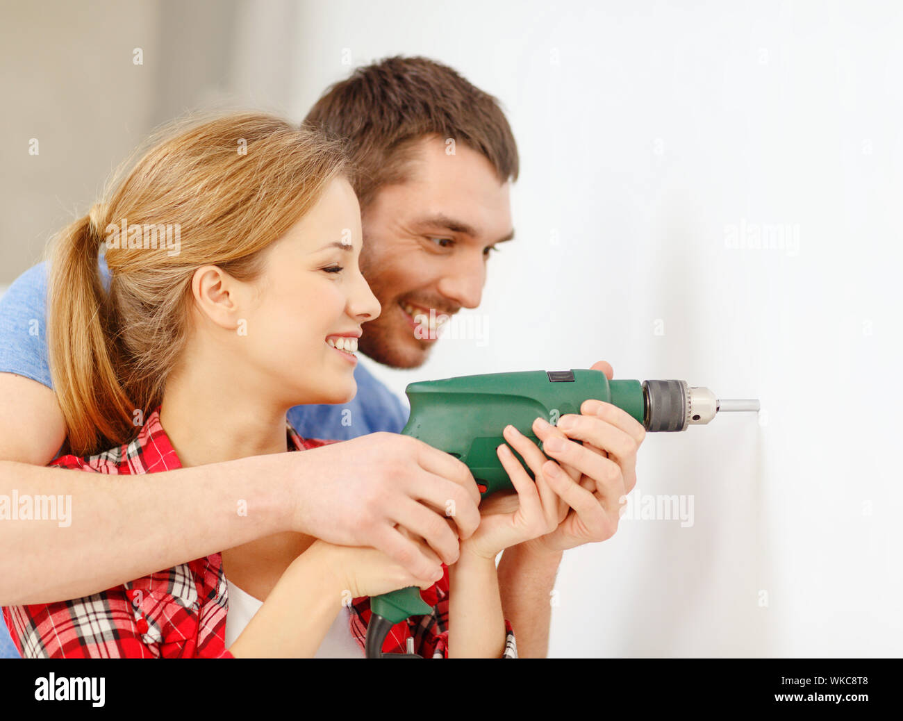 smiling couple drilling hole in wall at home Stock Photo - Alamy