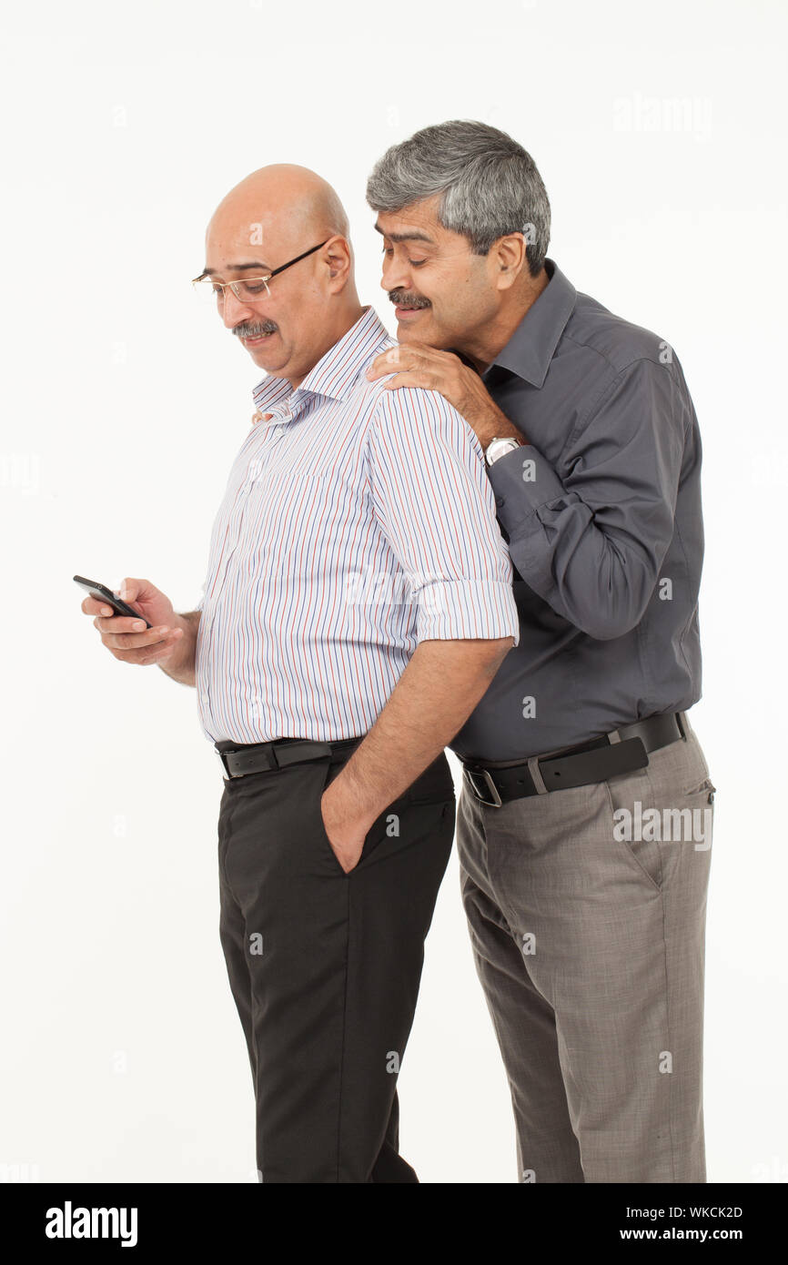 Man text messaging on a mobile phone with his friend standing behind ...