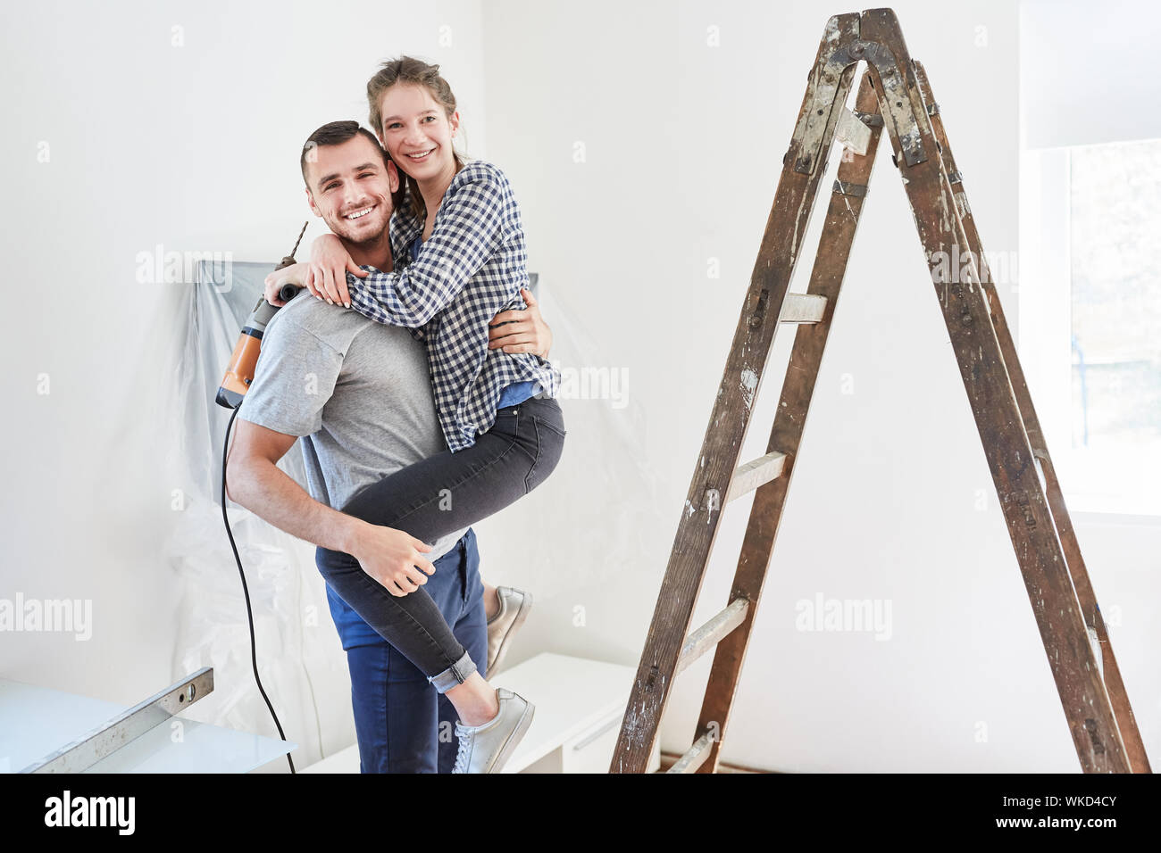 Amorous young couple with drill and ladder while renovating in new ...