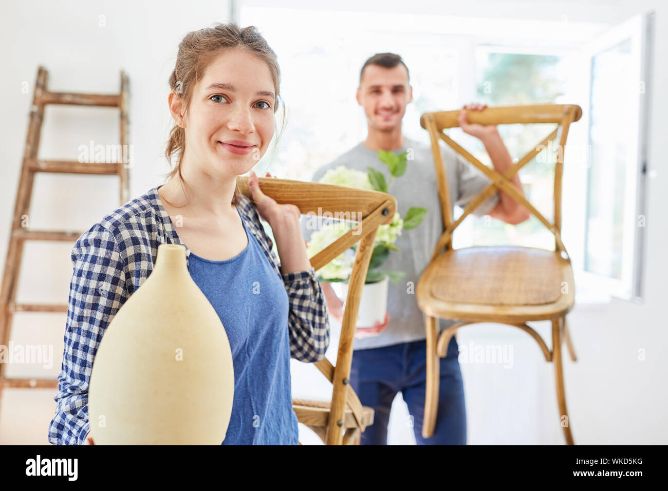 Young couple together carry chairs and a vase in the new home and pull ...