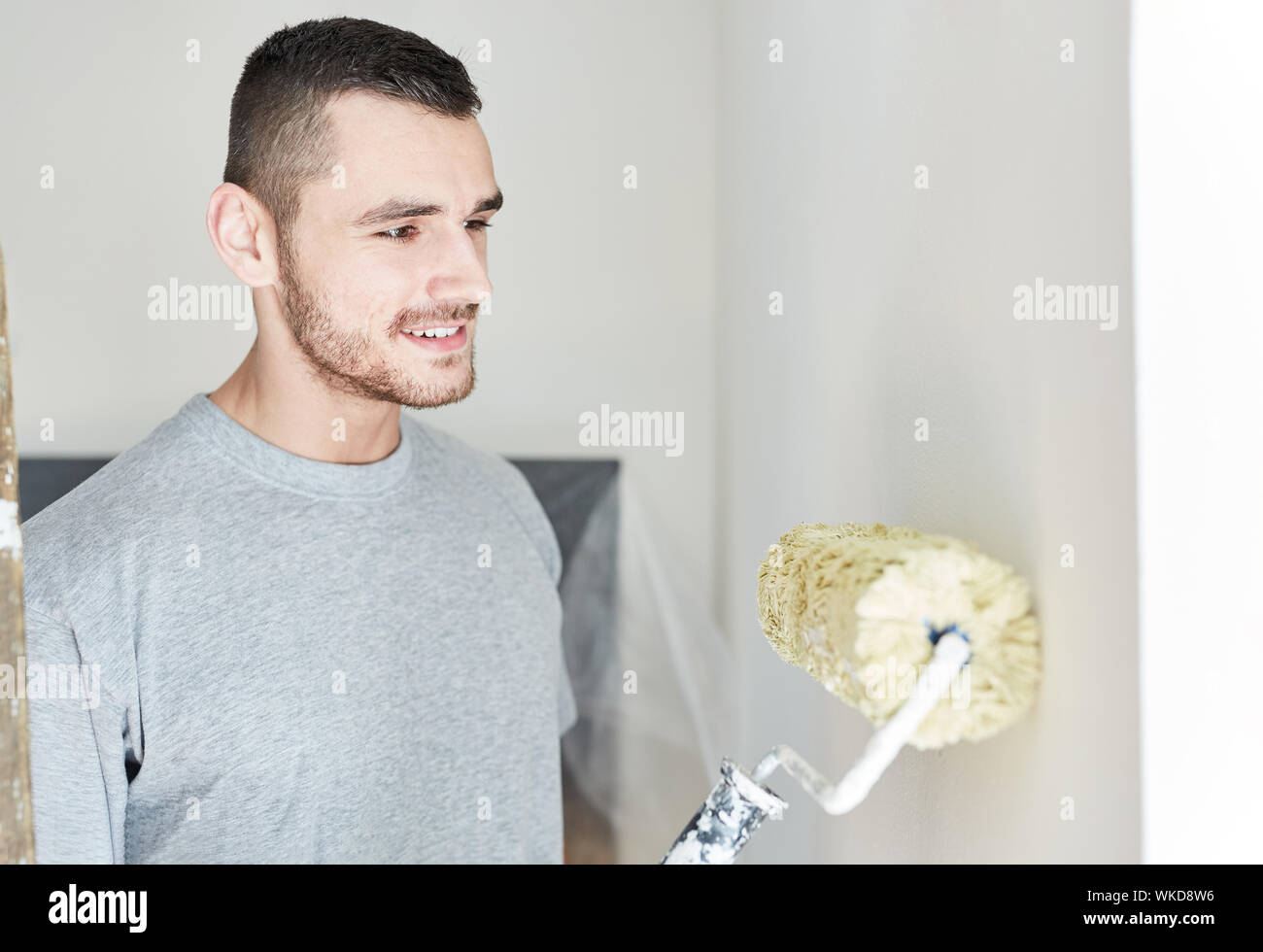 Young man with painter roll while painting walls and whites in new home ...