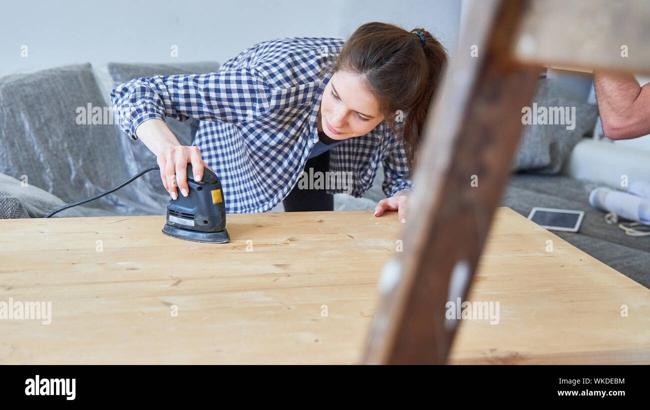 Young woman as a handyman with a multi-sander while sanding table for ...