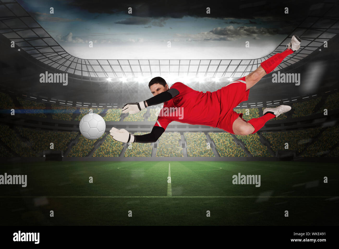 Fit goal keeper jumping up in a large football stadium with lights ...