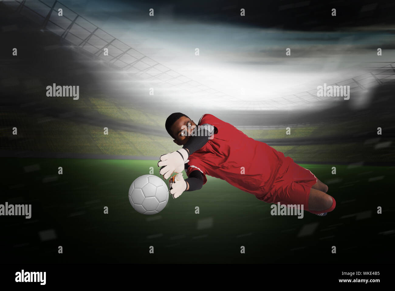 Goalkeeper in red making a save in a large football stadium with lights ...