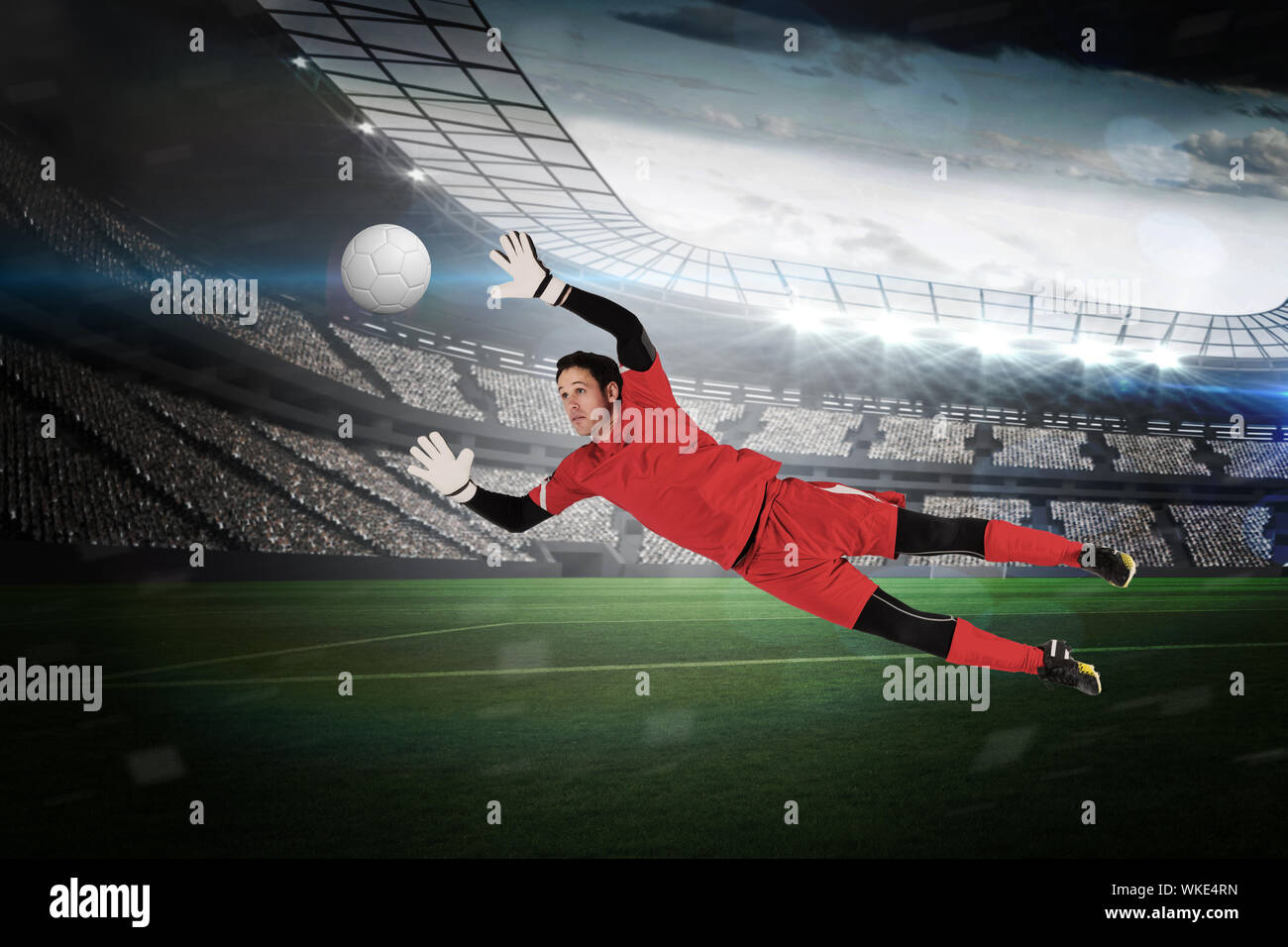 Fit goal keeper jumping up in a large football stadium with lights ...