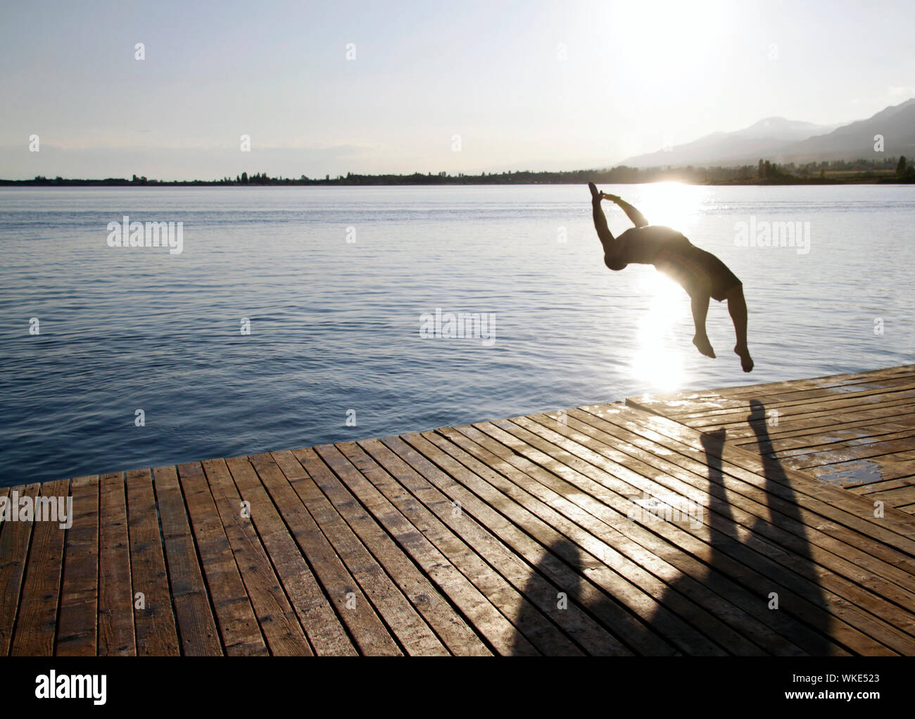 Silhouette of a boy jumping into water from a pier during sunset at ...
