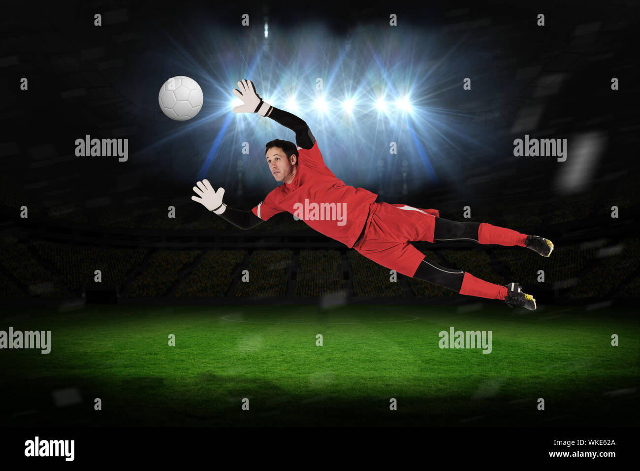 Fit goal keeper jumping up against football pitch under spotlights ...