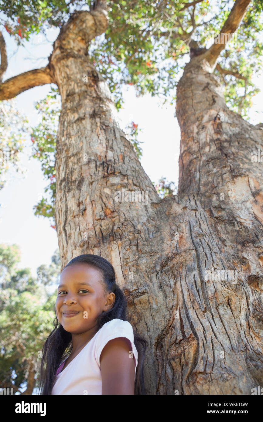 Little girl sitting by large tree smiling at camera on a sunny day ...