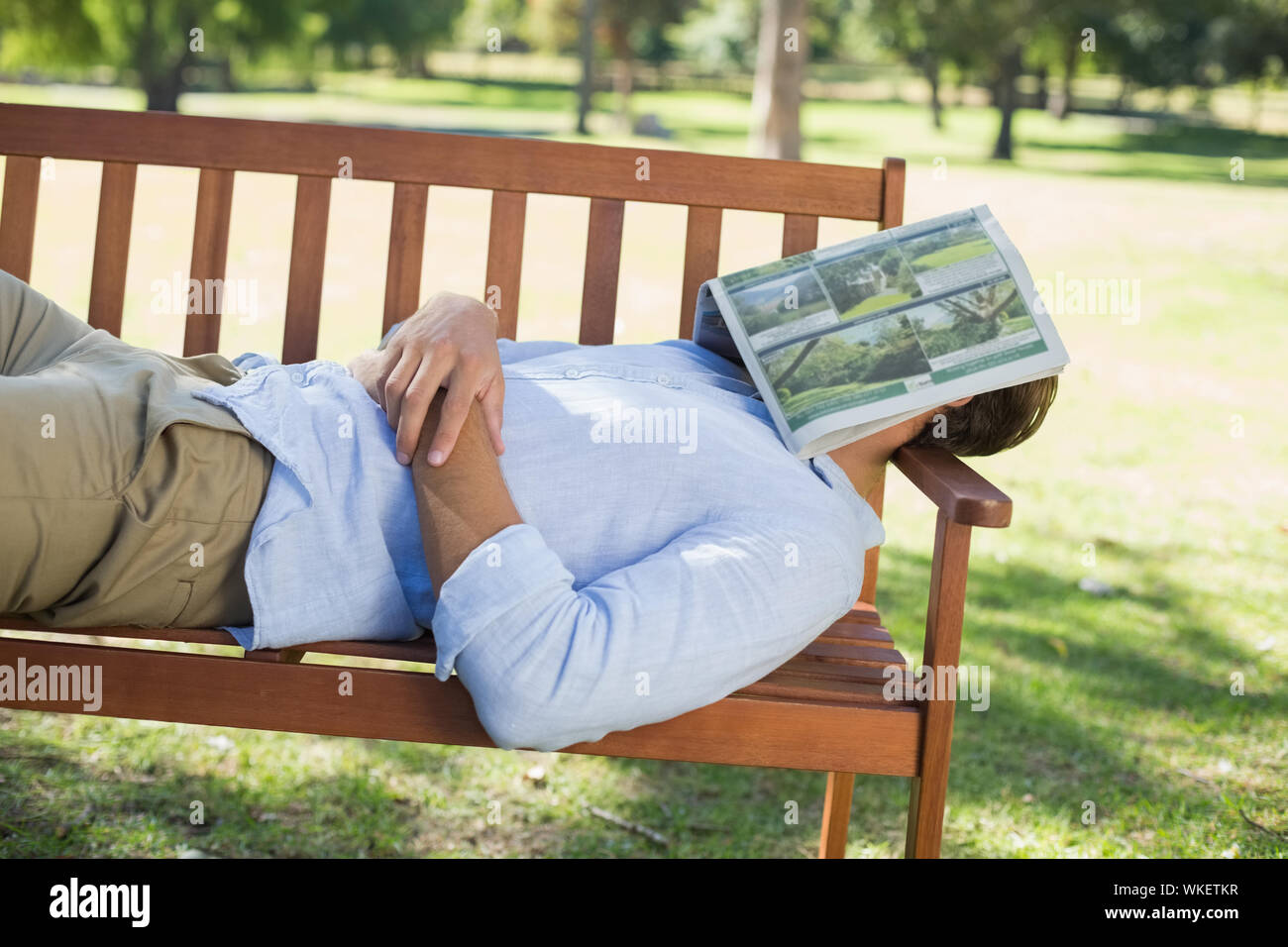 Man sleeping on park bench with newspaper over face on a sunny day ...