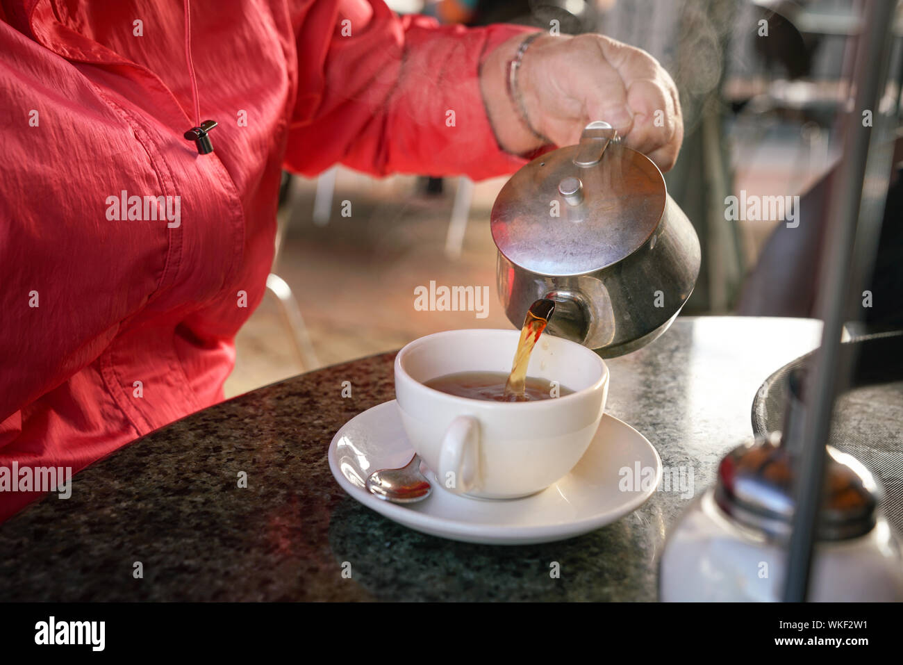 Hand pouring black tea from pot into white cup Stock Photo - Alamy
