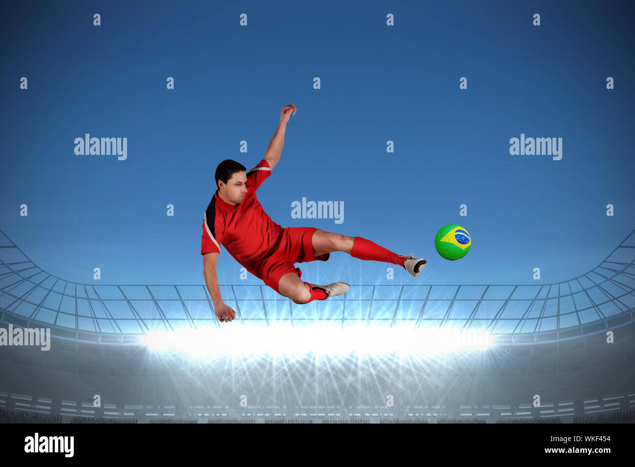 Fit football player jumping and kicking against large football stadium ...
