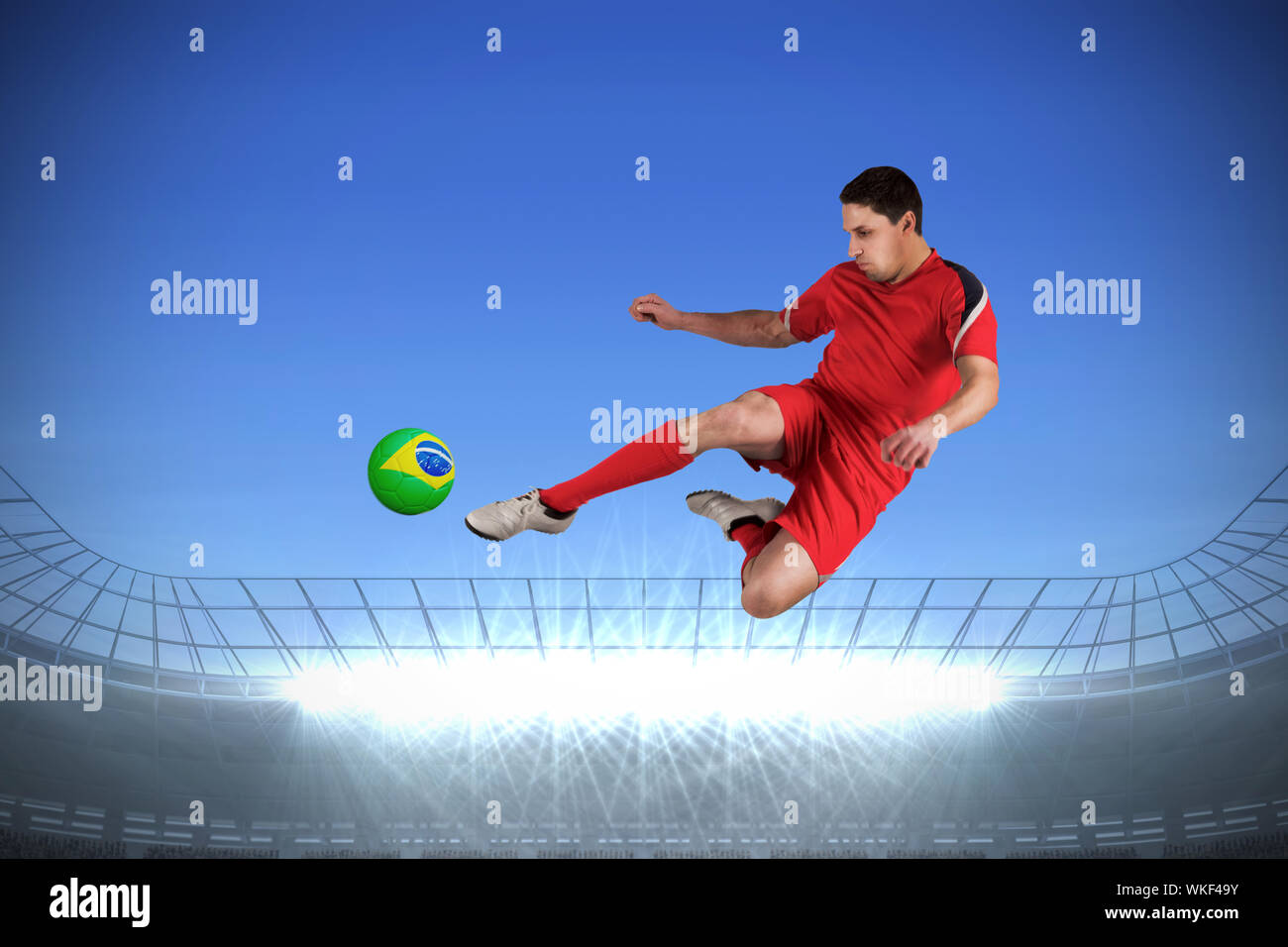 Fit football player jumping and kicking against large football stadium ...