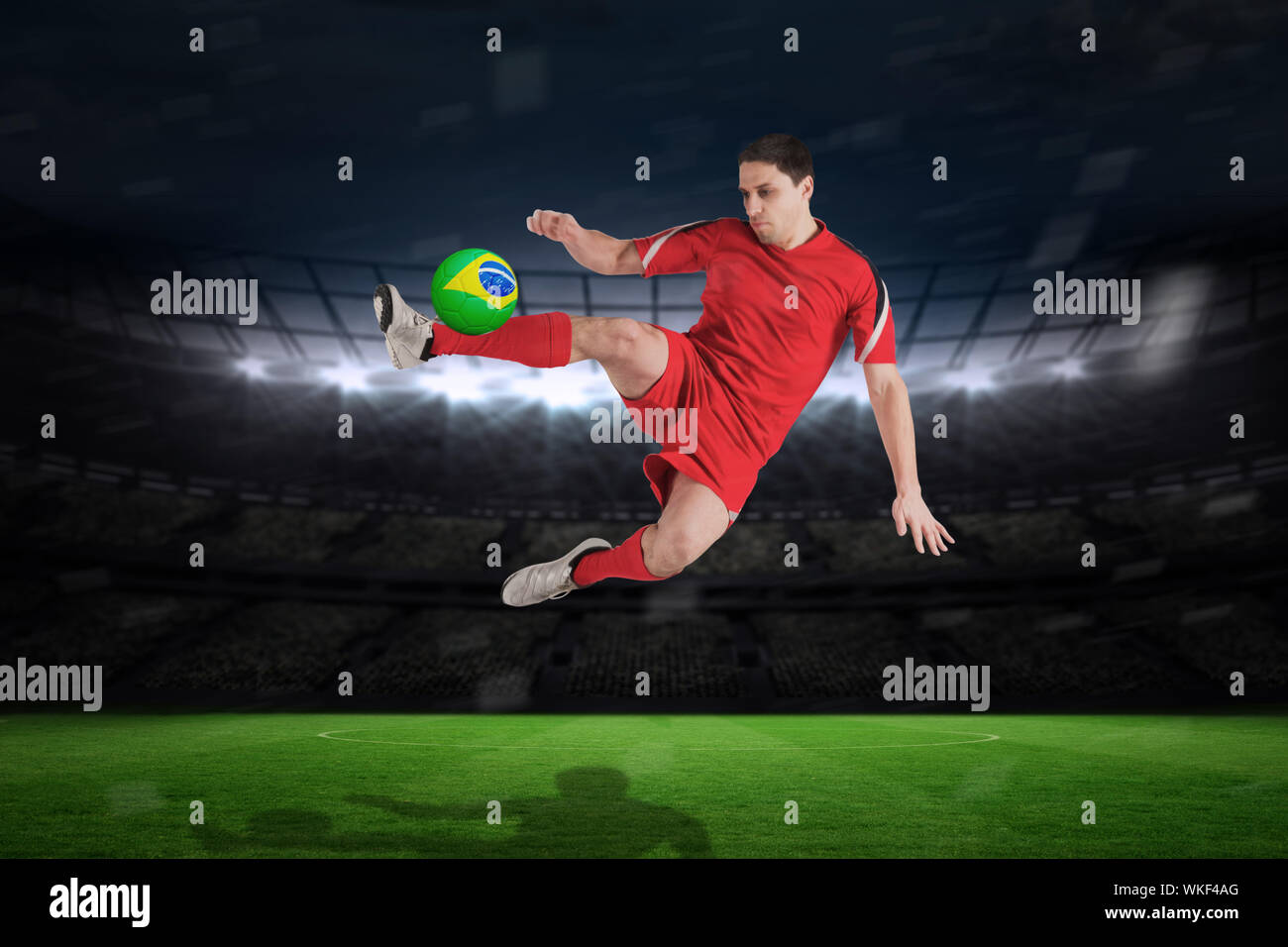 Fit football player jumping and kicking against large football stadium ...