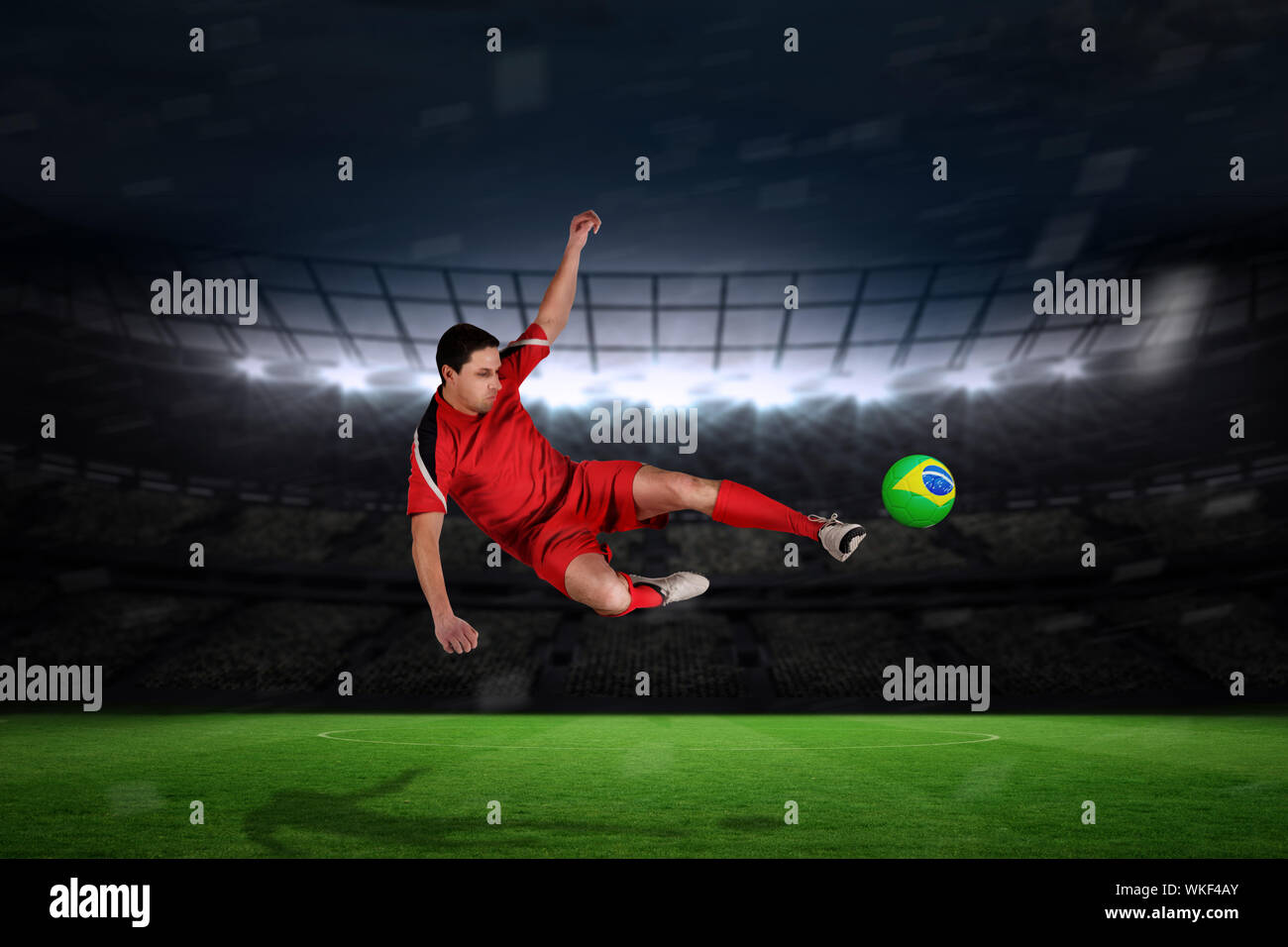 Fit football player jumping and kicking against large football stadium ...