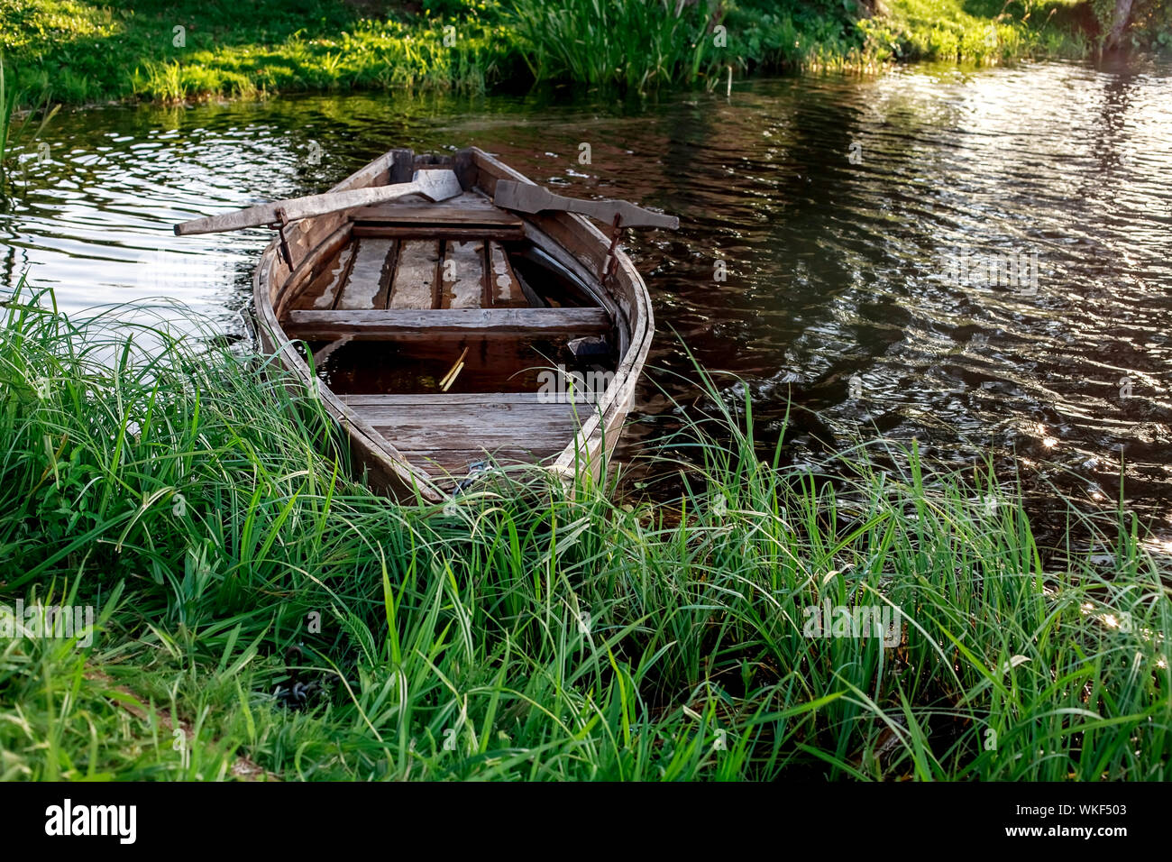 A small wooden rowing boat with a broken bottom on a calm lake near the ...