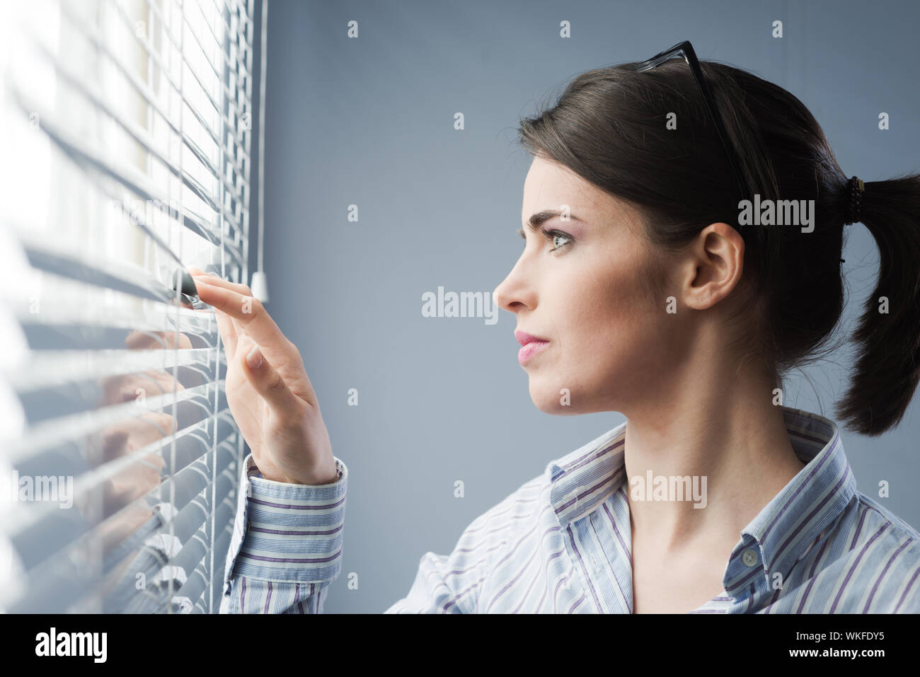 Young attractive woman peeking through blinds at window Stock Photo - Alamy