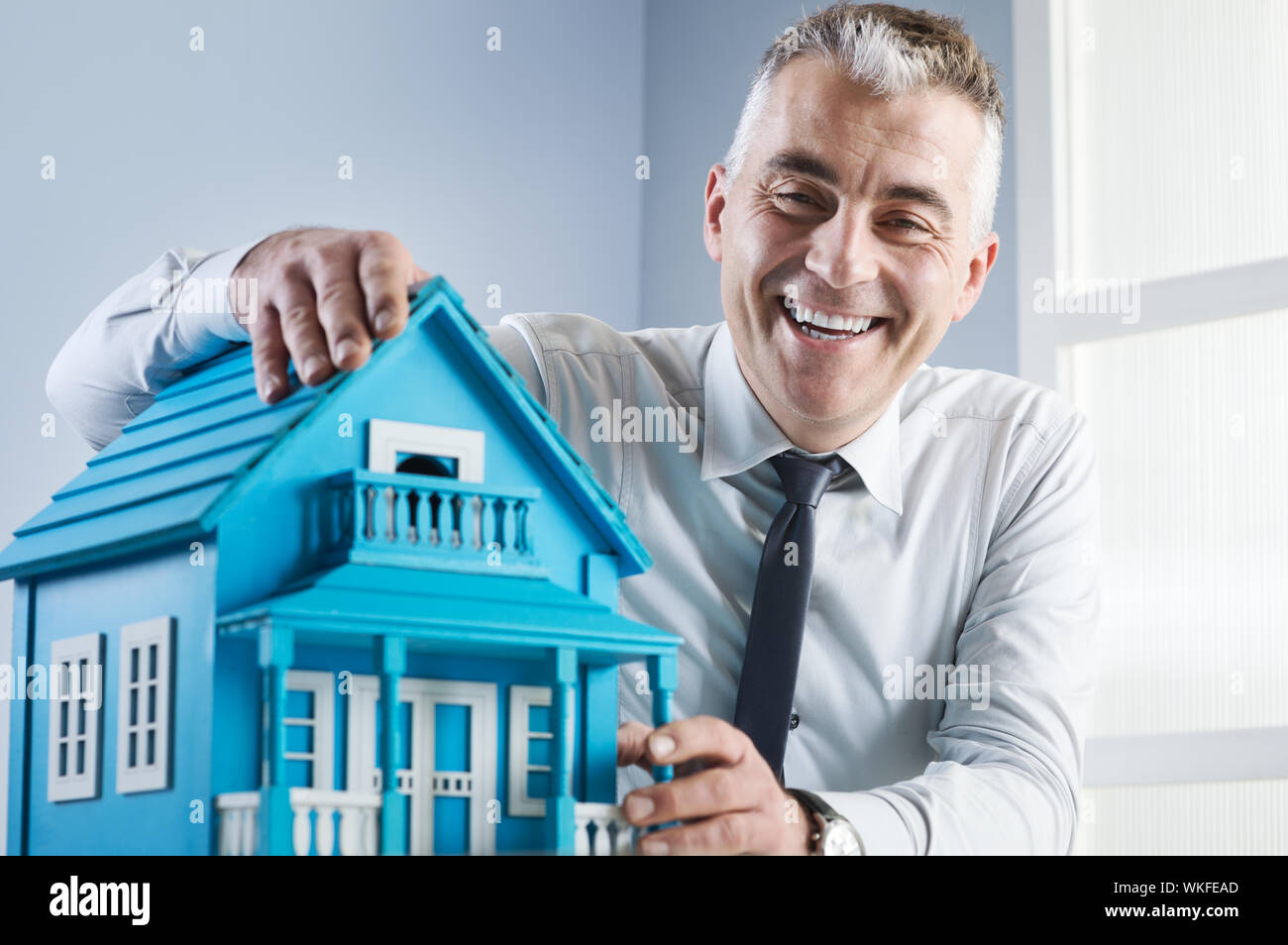 Real estate agent at desk with light blue model house Stock Photo - Alamy