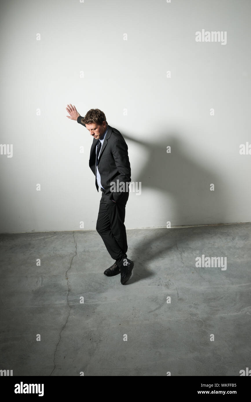 Tired pensive businessman leaning on a wall in an empty room with ...