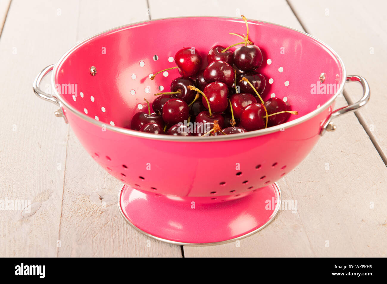 Cherries in pink colander on wooden underground Stock Photo - Alamy