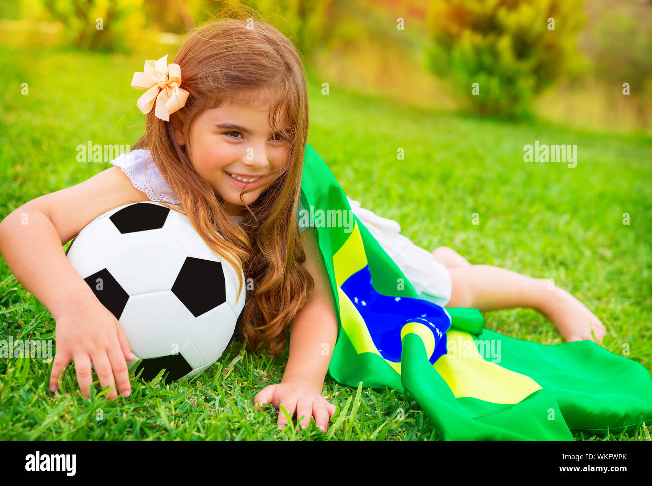 Young cheerful football fan lying down on fresh green grass with ball ...