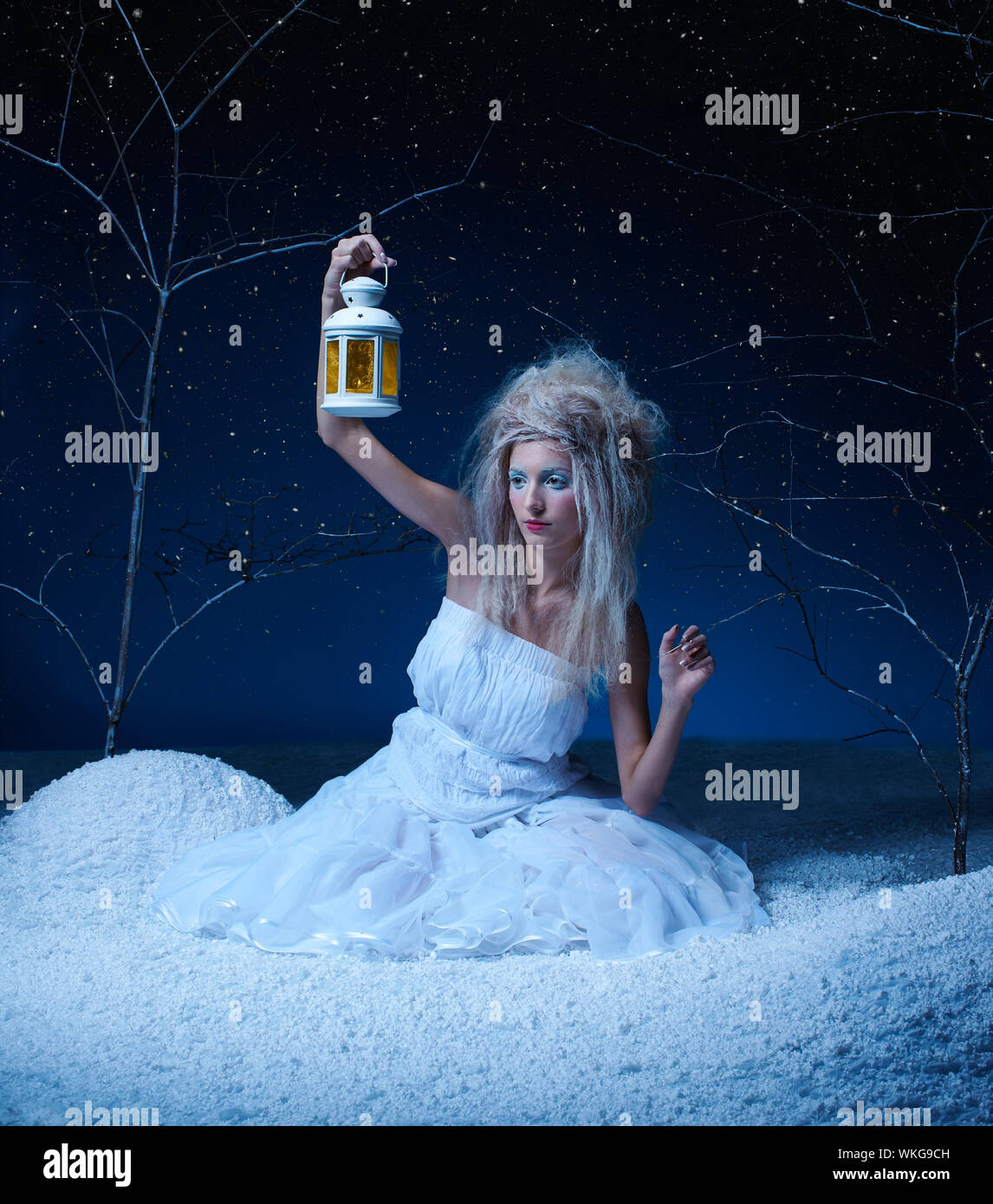 portrait of beautiful frozen fairy nymph girl sitting on snow with lamp ...