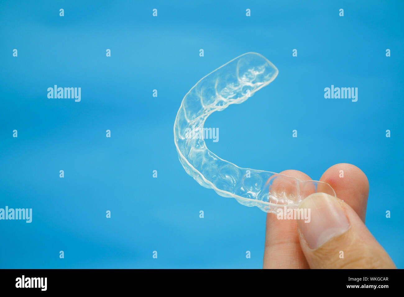 hand holding clear plastic retainer teeth that isolated on blue sky ...