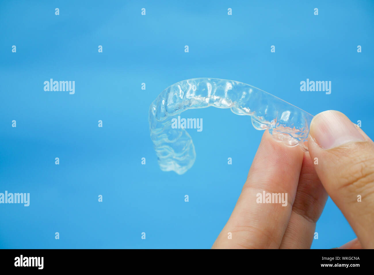 hand holding clear plastic retainer teeth that isolated on blue sky ...