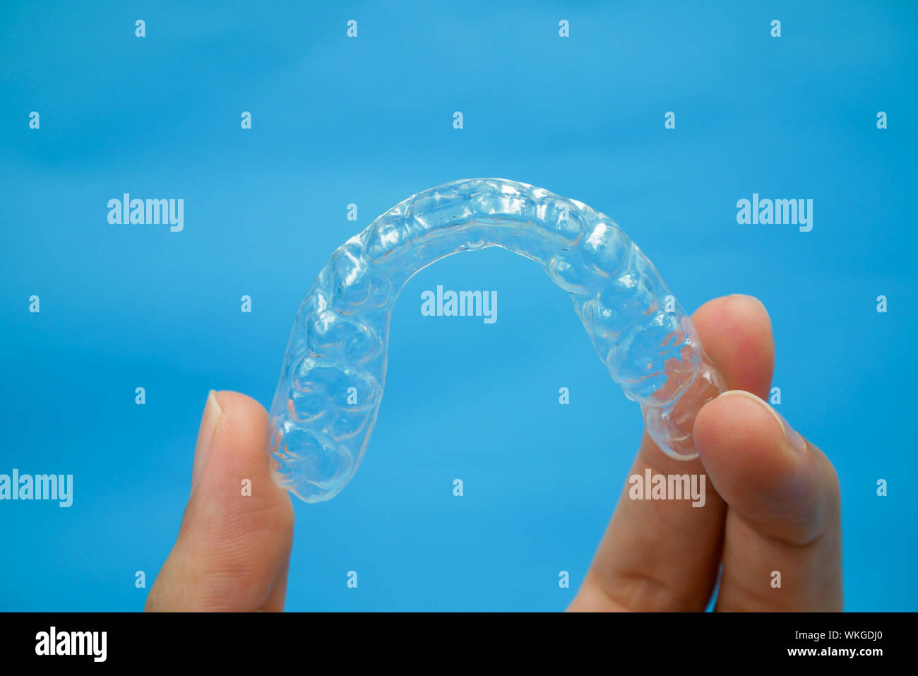 hand holding clear plastic retainer teeth that isolated on blue sky ...