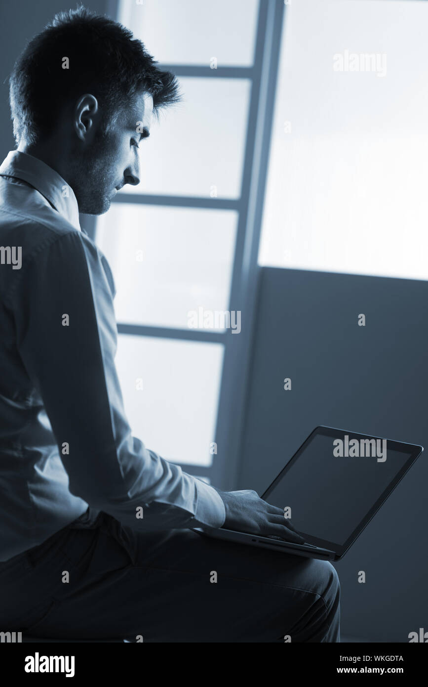 Young man sitting and working with laptop on his lap Stock Photo - Alamy