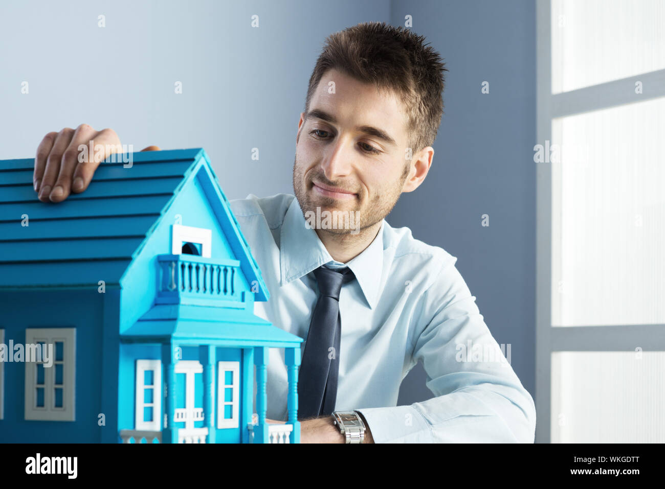 Friendly real estate agent with light blue model house Stock Photo - Alamy