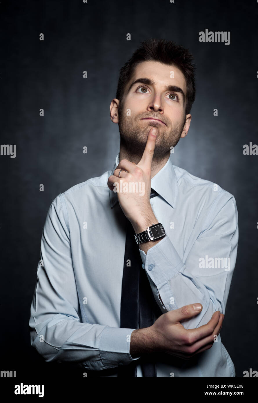 Young man thinking with finger on his chin on dark background Stock ...