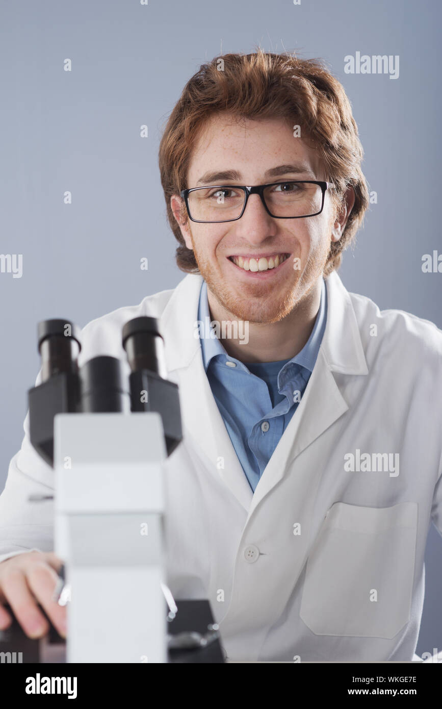 Student researcher using microscope and smiling at camera Stock Photo ...