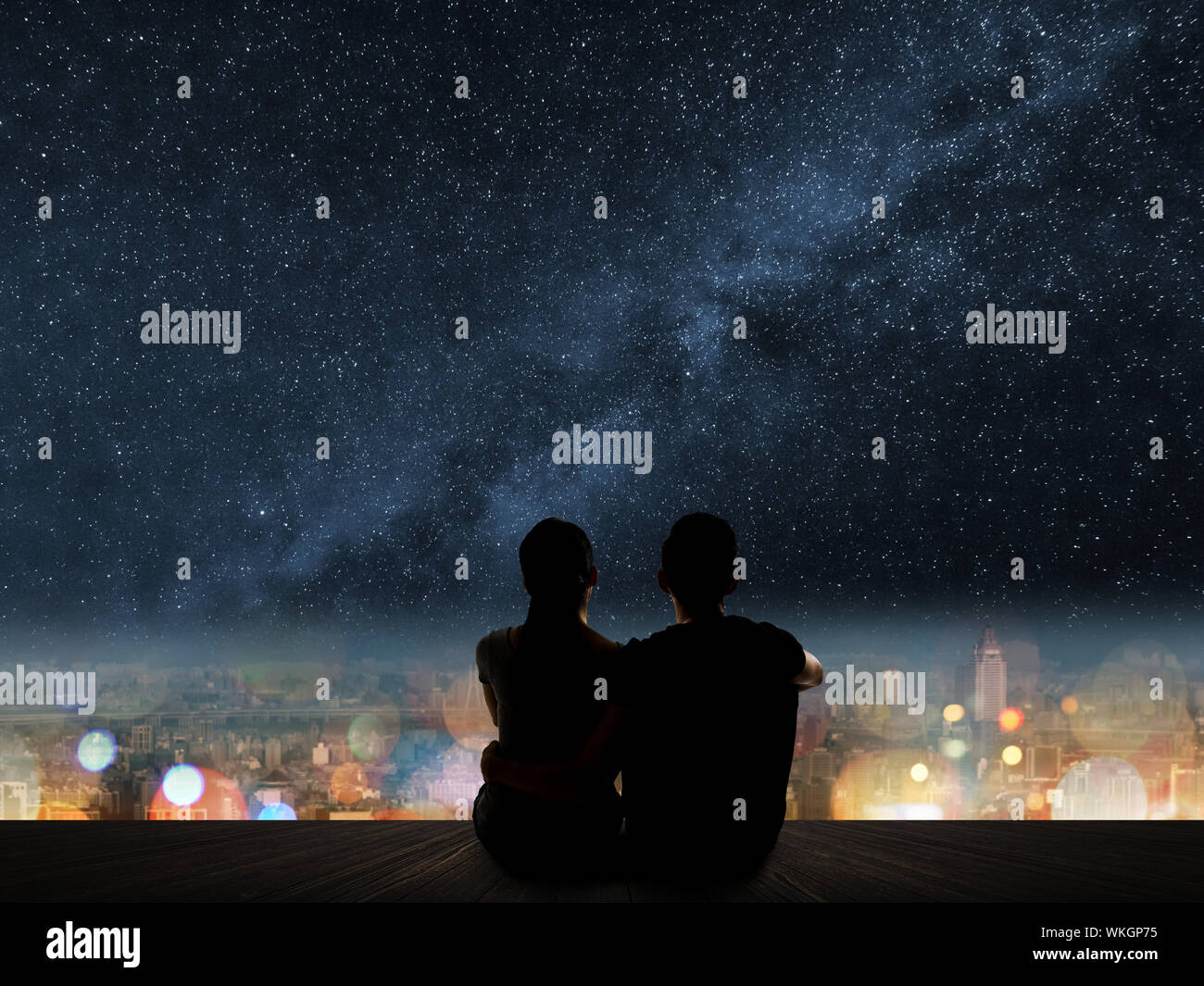 Silhouette of young Asian couple sit on wooden ground above the city ...