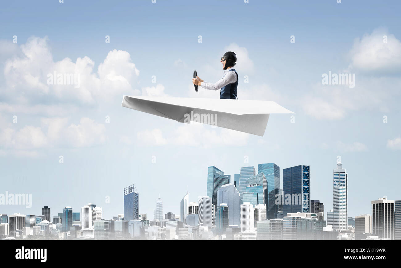Aviator driving paper plane above business center in cloudy blue sky ...
