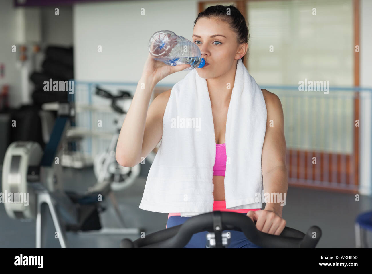 Tired young woman drinking water while working out at spinning class in ...