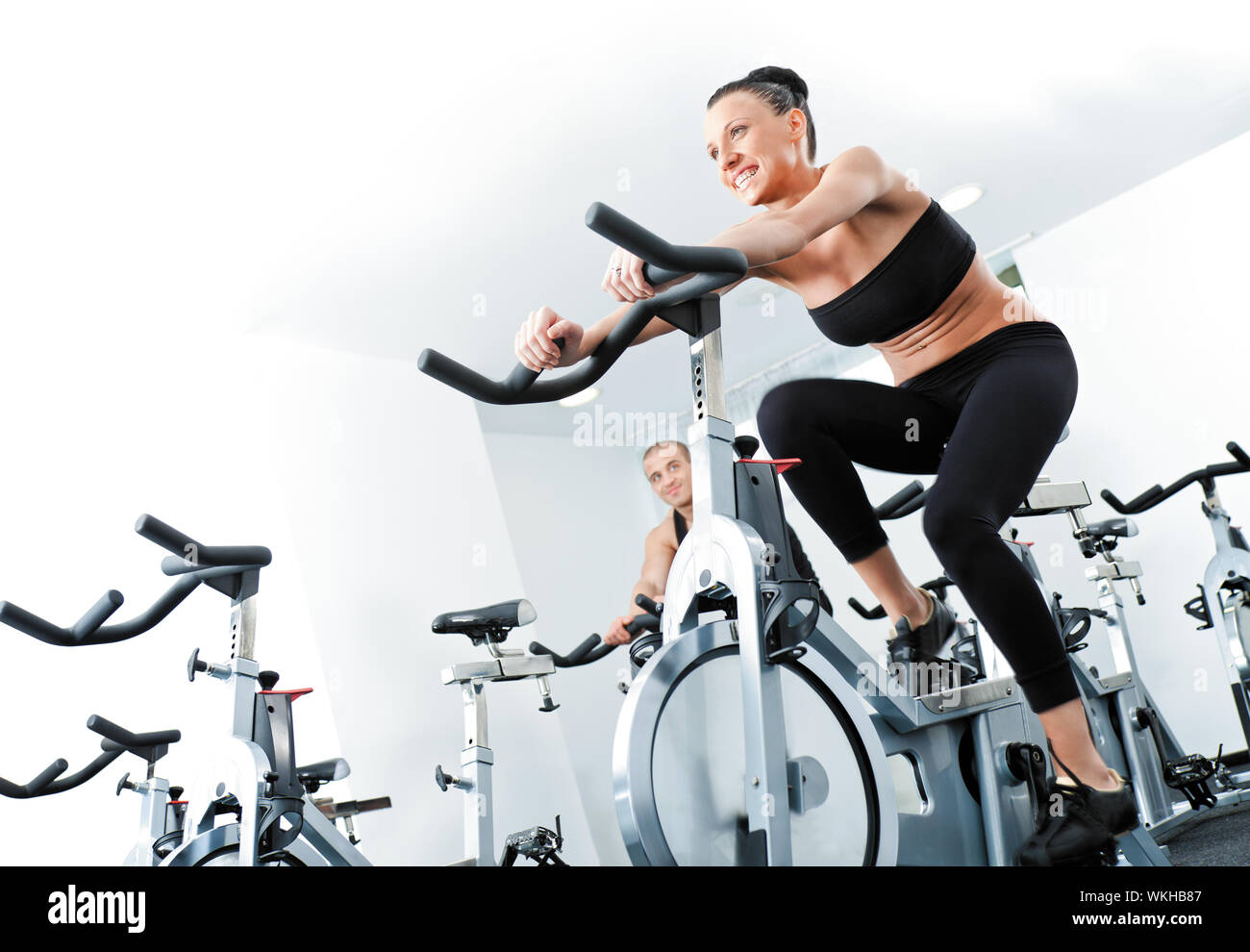 Young athletic female spinning veloargometers in gym, male behind Stock ...