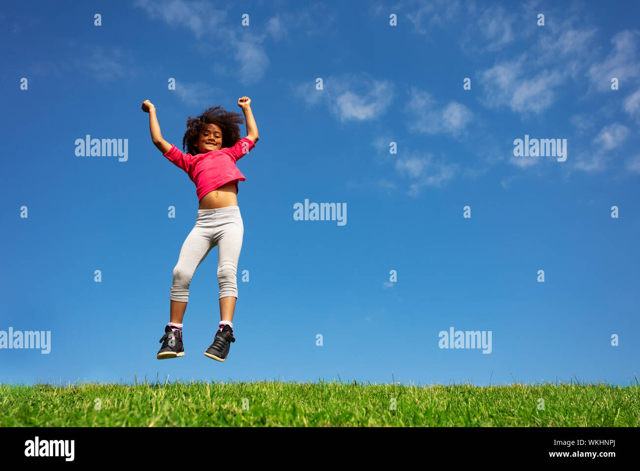 Happy curly hair girl jump over blue sky hands up Stock Photo - Alamy