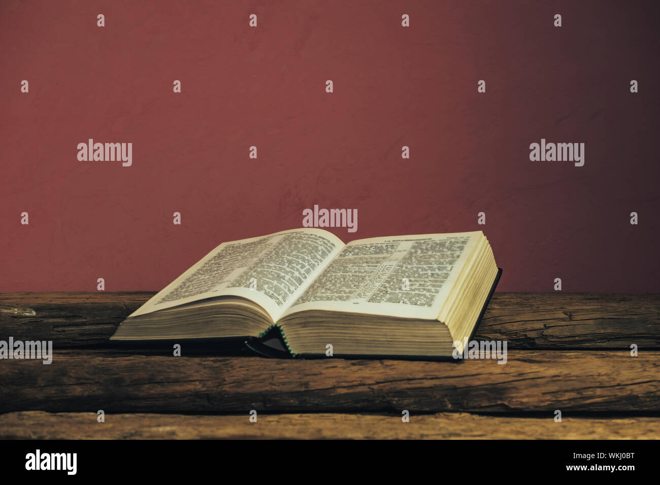 Beautiful open Holy Bible on old oak wooden table and dark red wall ...