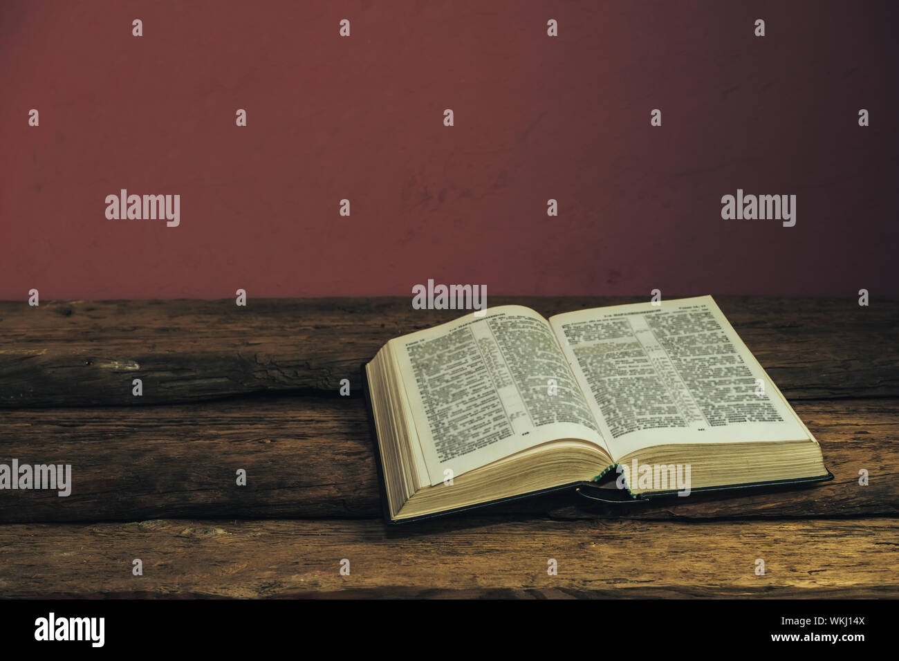 Beautiful open Holy Bible on old oak wooden table and dark red wall ...