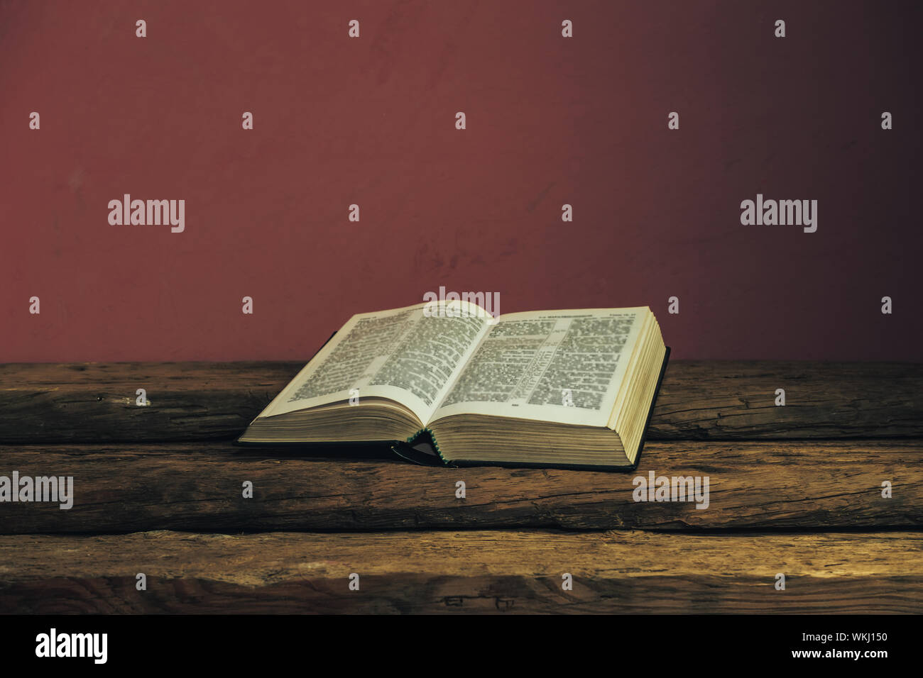 Beautiful open Holy Bible on old oak wooden table and dark red wall ...