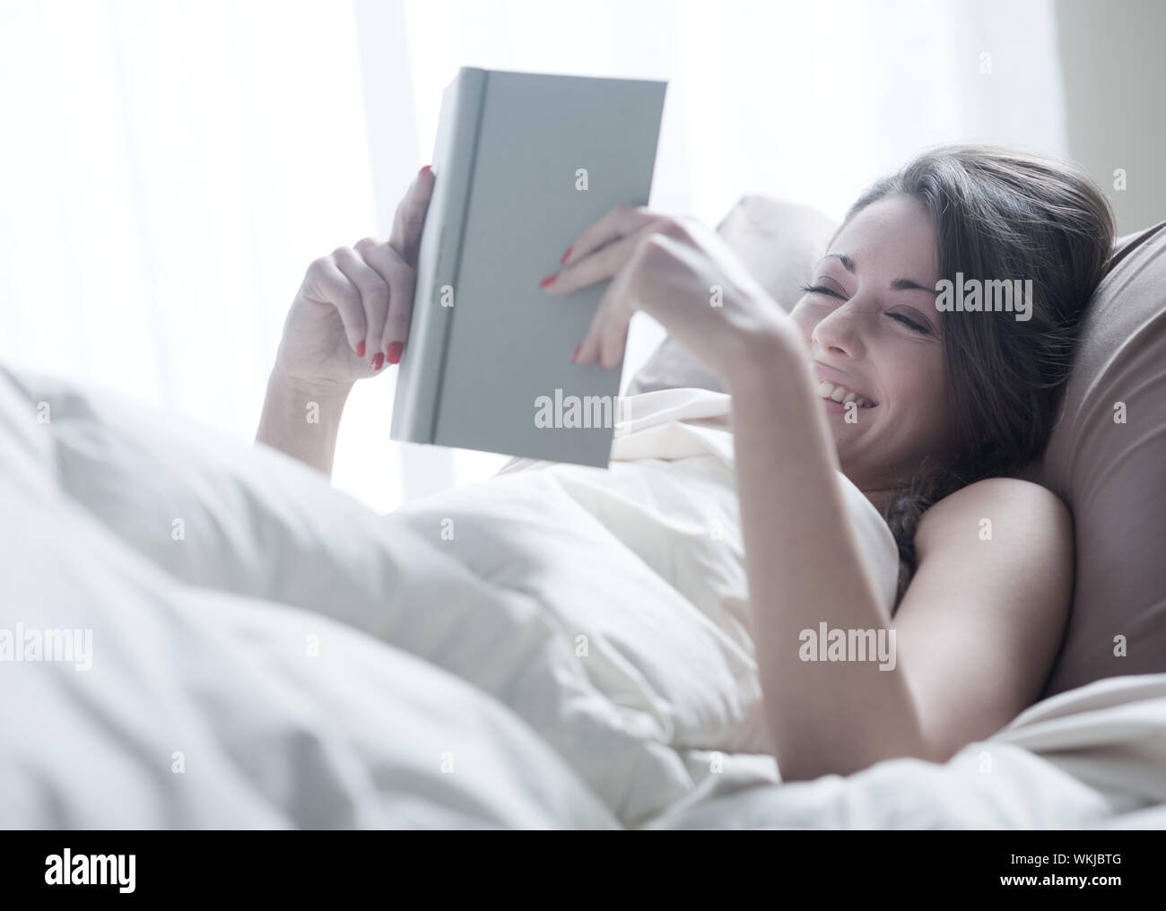 Woman lying in bed while reading a book Stock Photo - Alamy