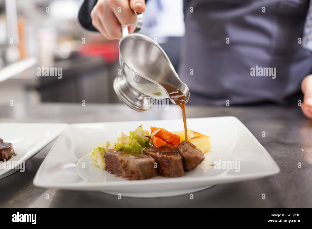 Chef plating up food in a restaurant pouring a gravy or sauce over the ...