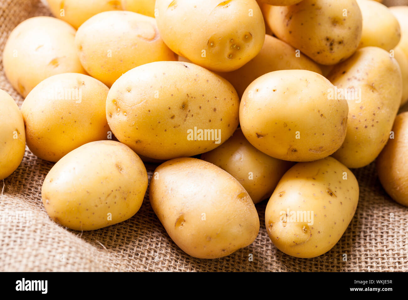 Farm fresh baby potatoes displayed on a hessian sack on a rustic wooden ...