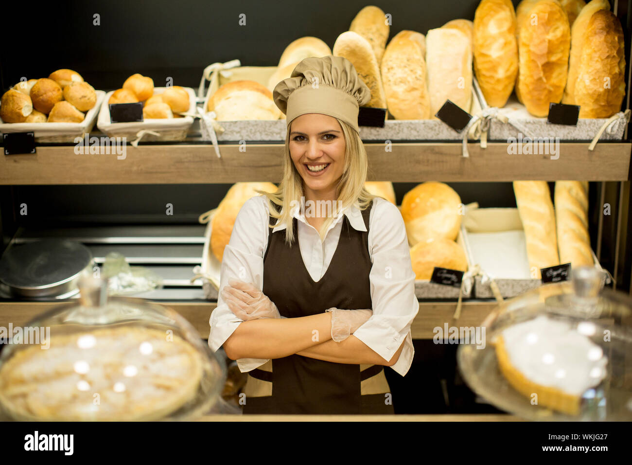 Portrait of friendly female baker with fresh bread smiling in bakery ...