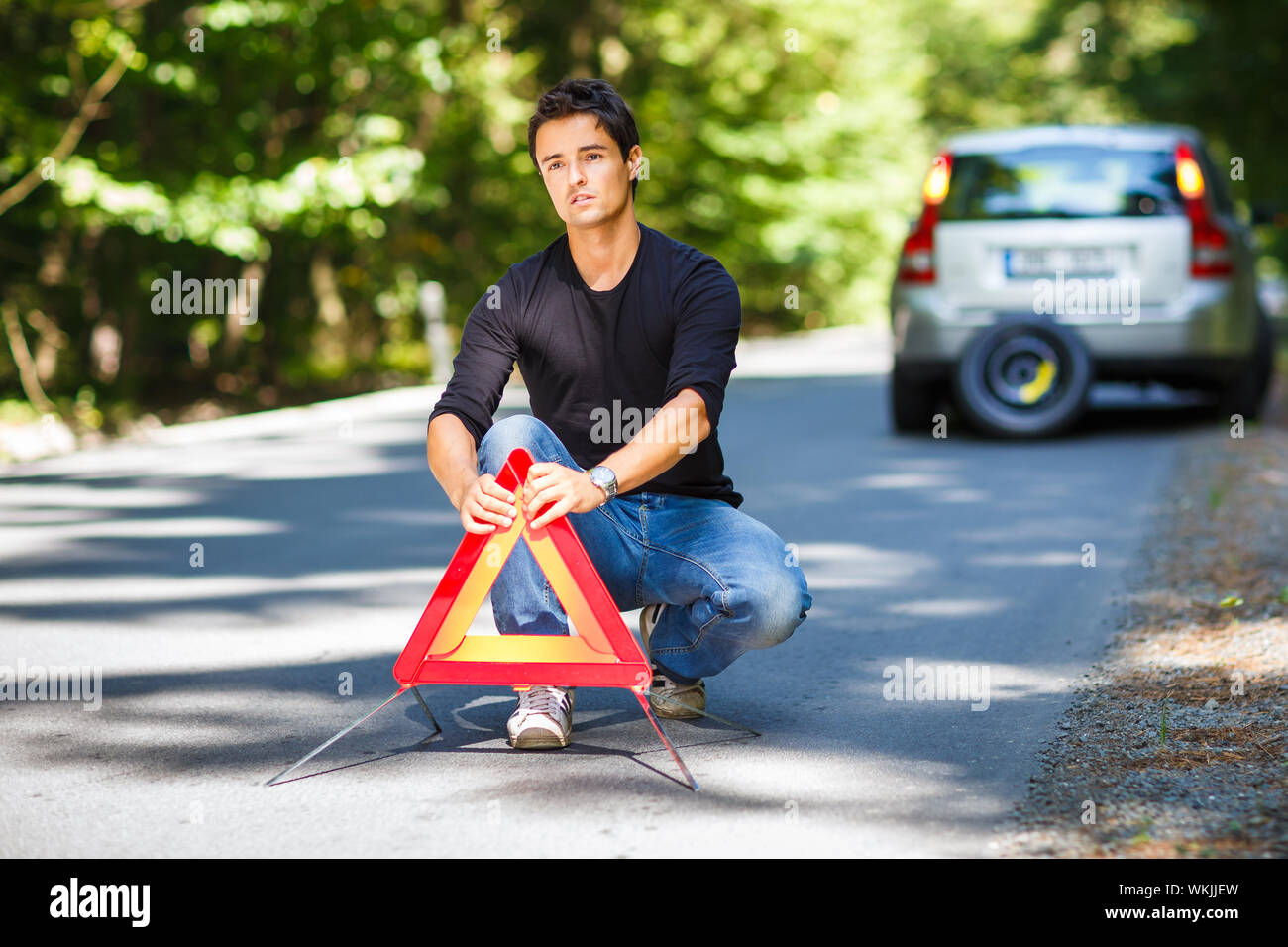 Handsome young man with his car broken down by the roadside, setting ...